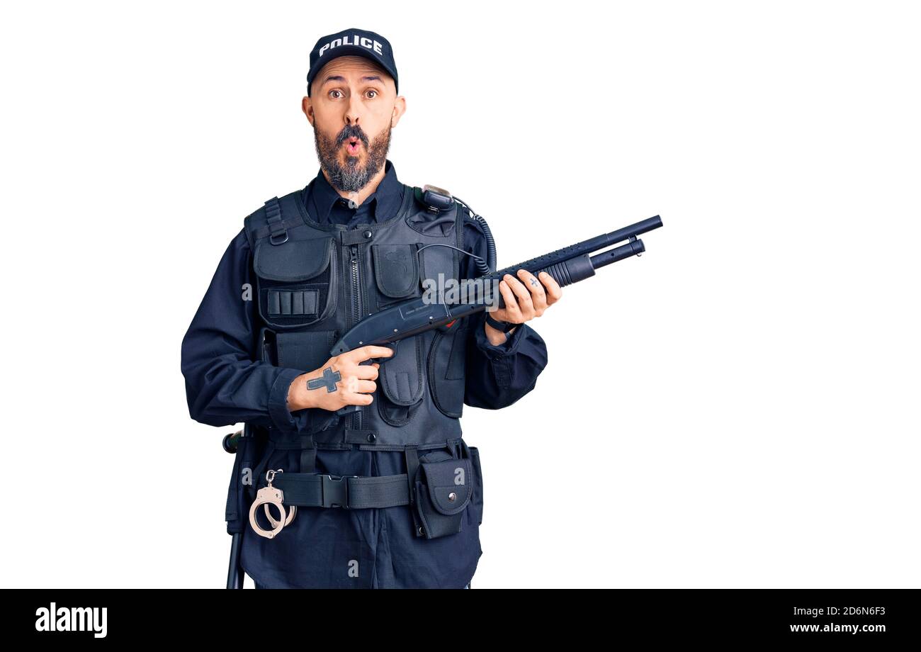 Young handsome man wearing police uniform holding shotgun scared and ...