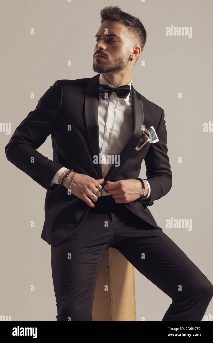 Confident groom unbuttoning his jacket and looking away, wearing tuxedo ...