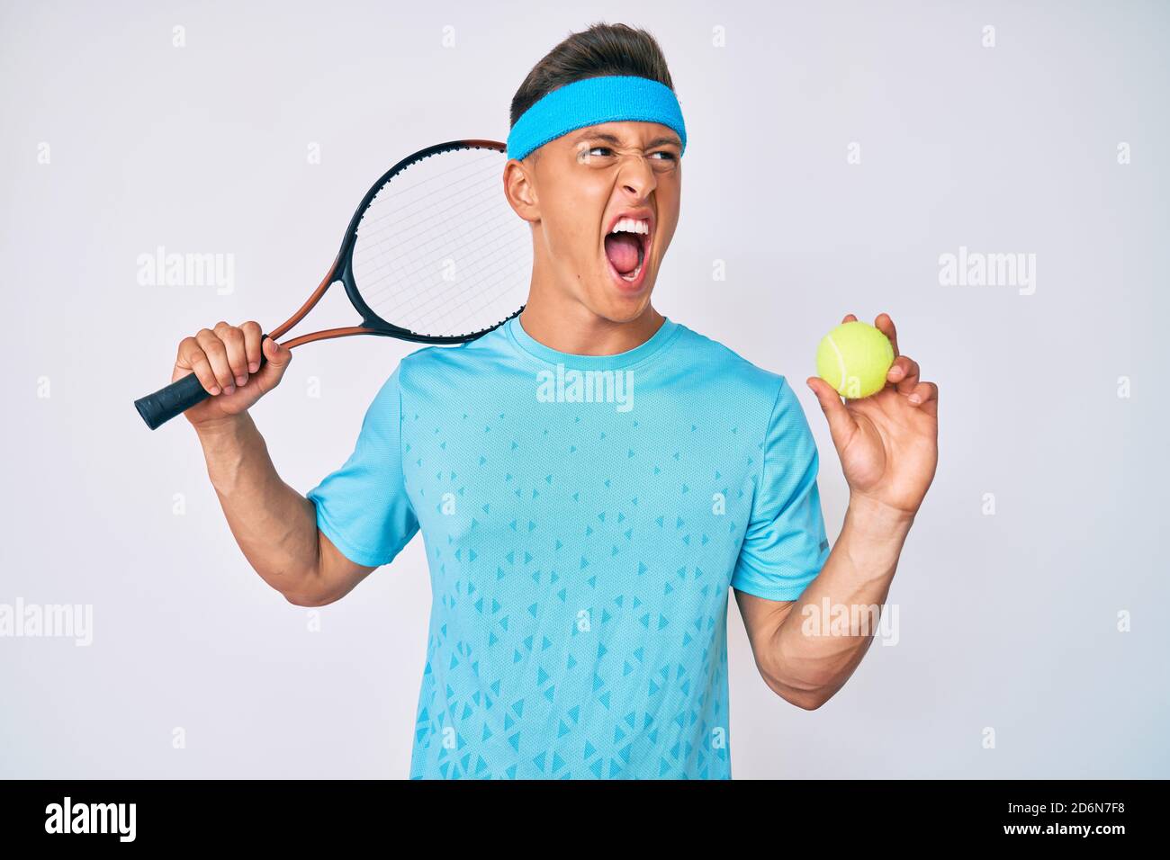Young hispanic boy playing tennis holding racket and ball angry and mad ...