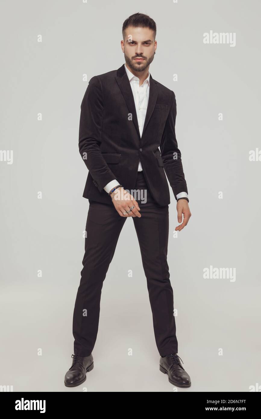 Tough fashion model wearing suit and standing on gray studio background ...