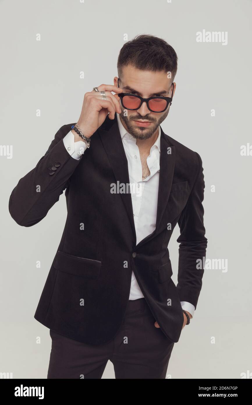 Confident fashion model taking off sunglasses with hand in pocket while ...