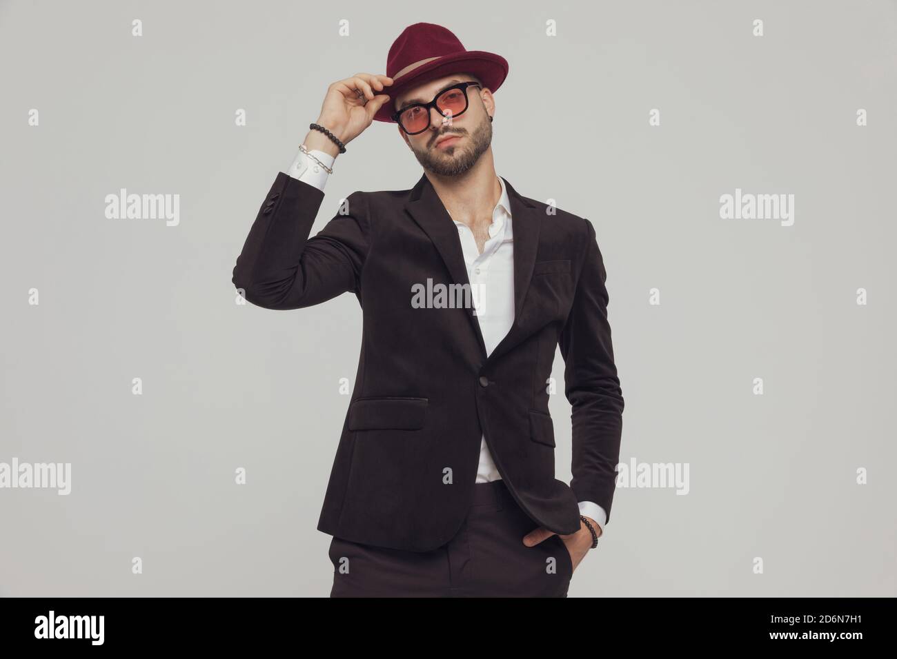 Confident fashion model taking off hat with hand in pocket, wearing ...