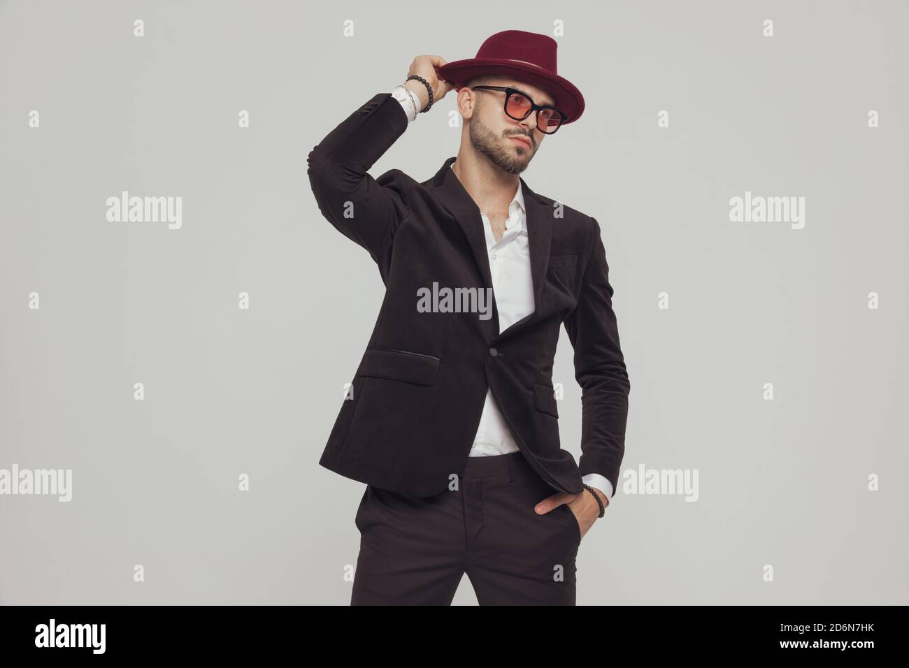 Confident fashion model fixing hat with hand in pocket, wearing ...