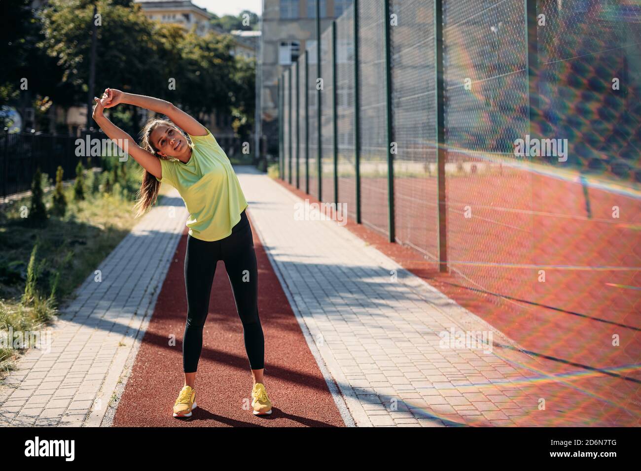 Fitness young lady stretching body while standing at stadium Stock ...
