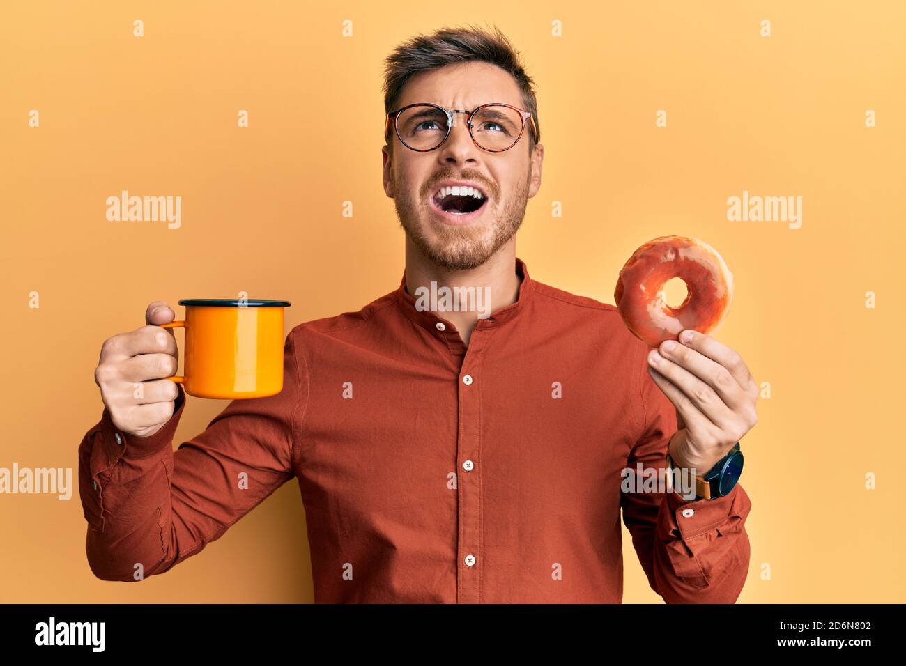 Handsome caucasian man eating doughnut and drinking coffee angry and ...