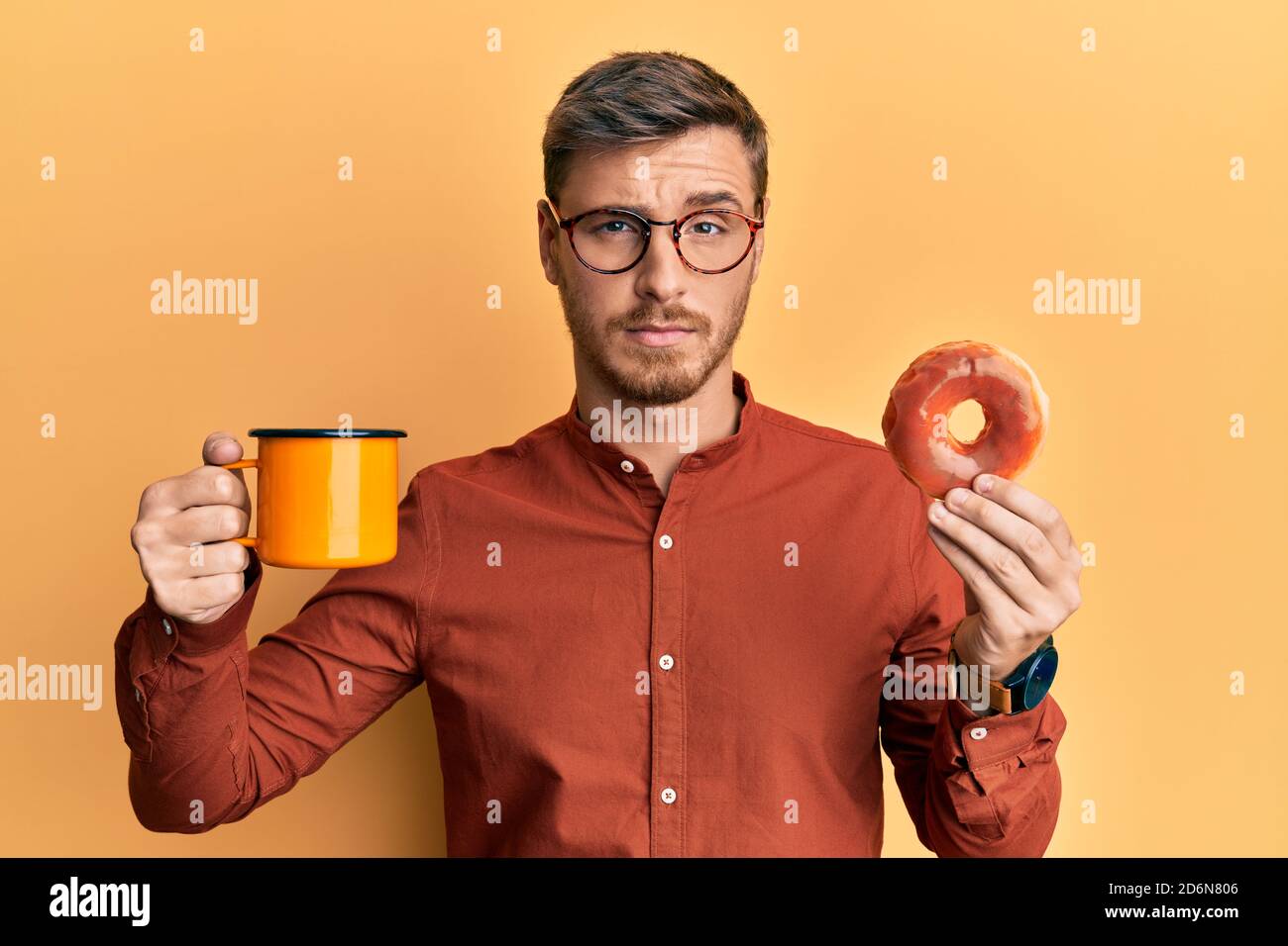 Handsome caucasian man eating doughnut and drinking coffee skeptic and ...