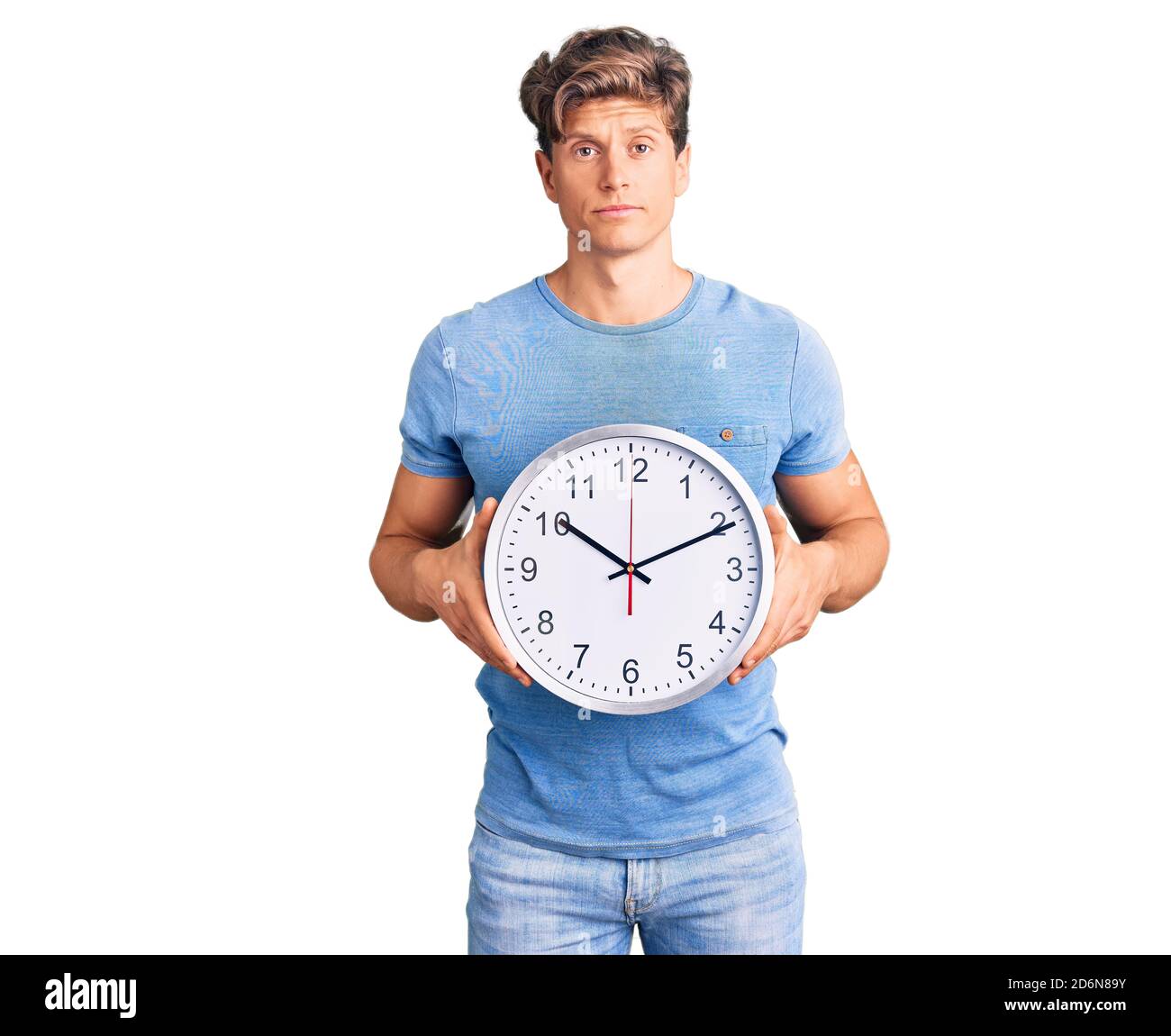 Young handsome man holding big clock thinking attitude and sober ...