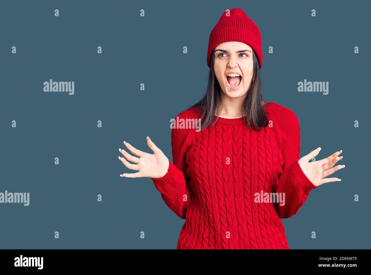 Young beautiful girl wearing sweater and wool cap crazy and mad ...