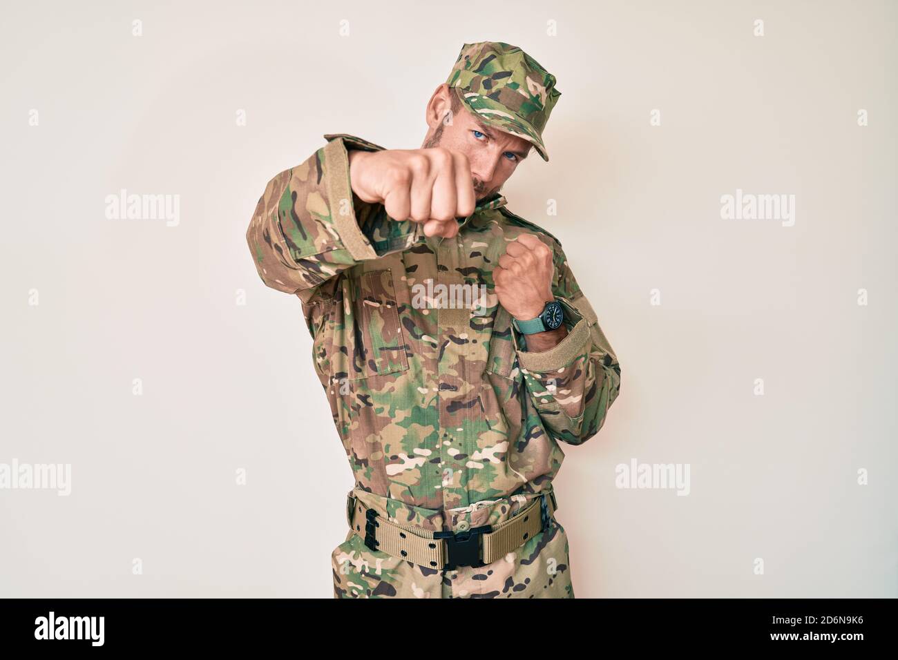 Young caucasian man wearing camouflage army uniform punching fist to ...