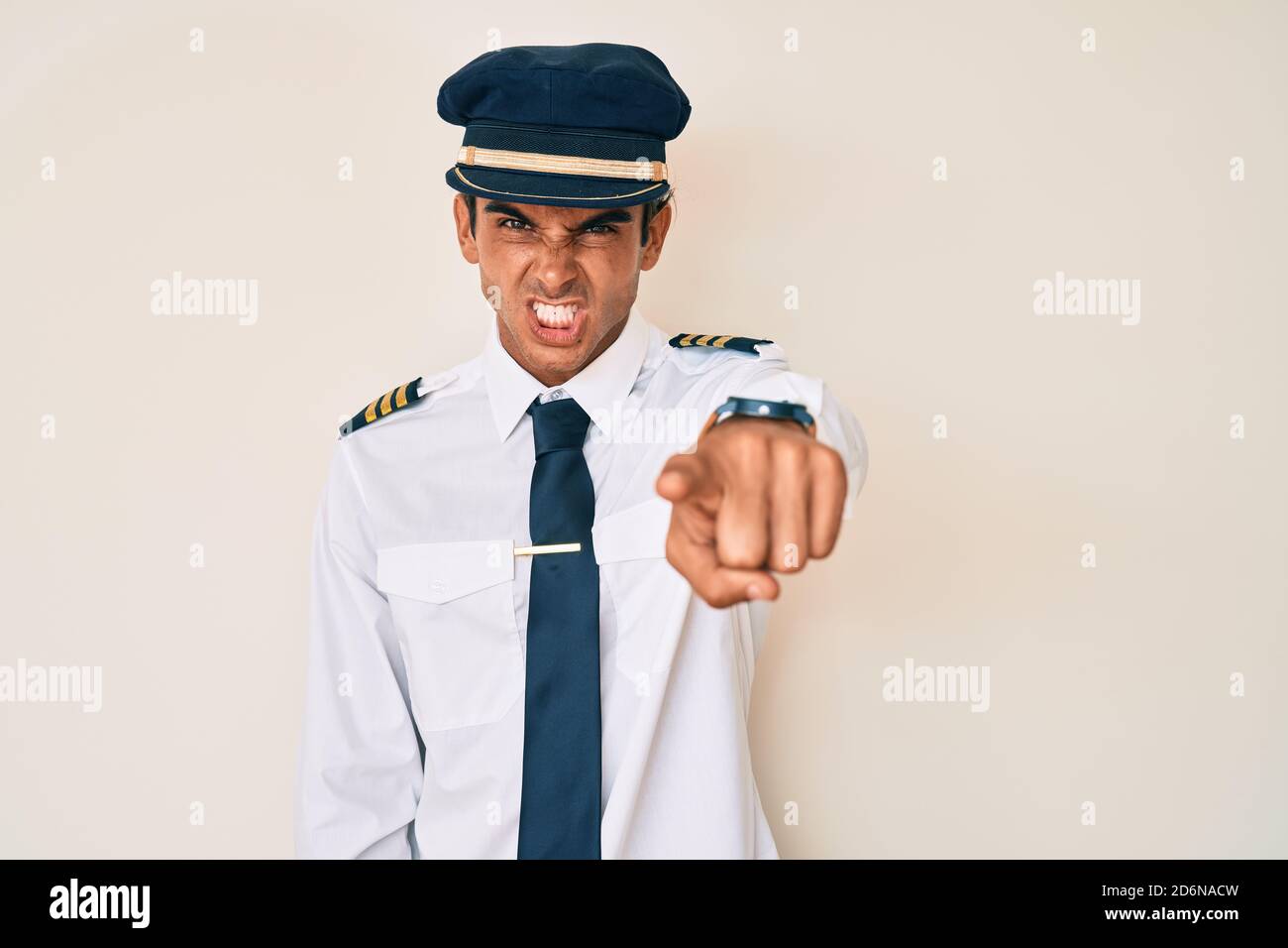 Young hispanic man wearing airplane pilot uniform pointing displeased ...