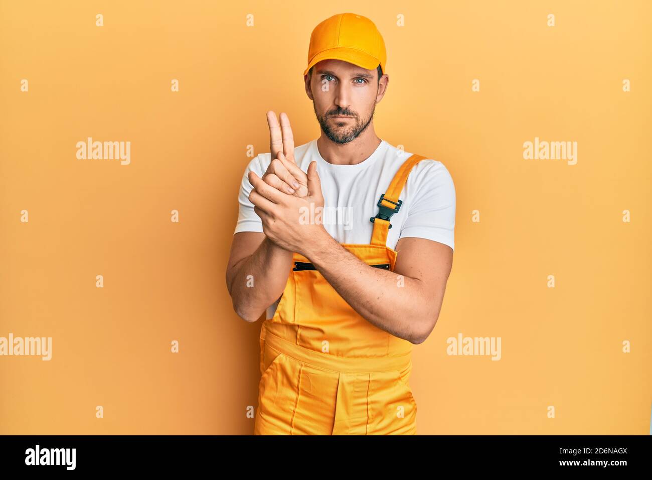 Young handsome man wearing handyman uniform over yellow background ...