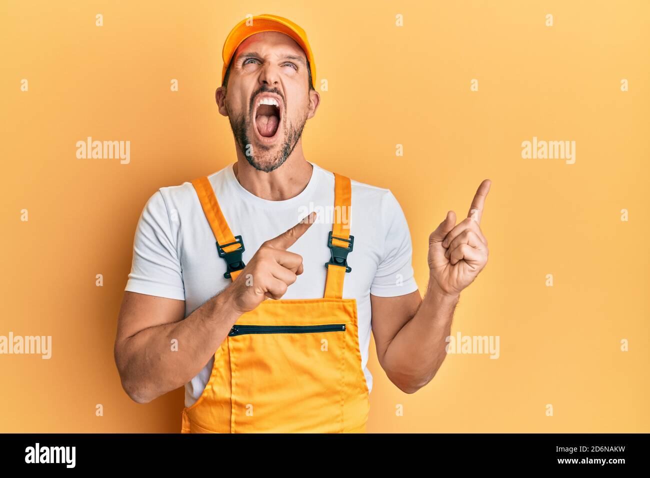 Young handsome man wearing handyman uniform pointing to the side angry ...