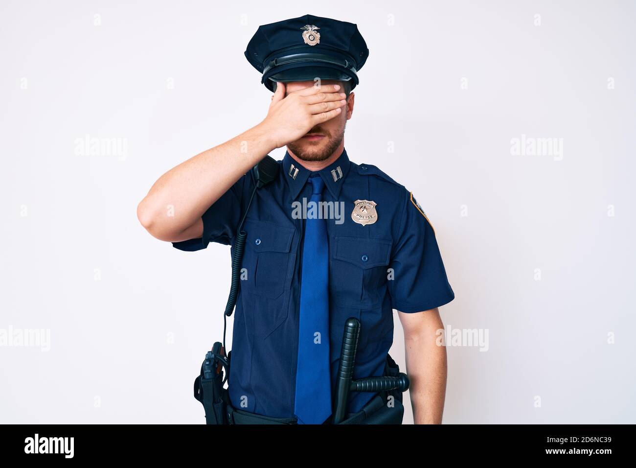 Young caucasian man wearing police uniform covering eyes with hand ...