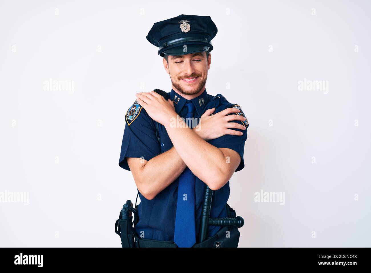 Young caucasian man wearing police uniform hugging oneself happy and ...