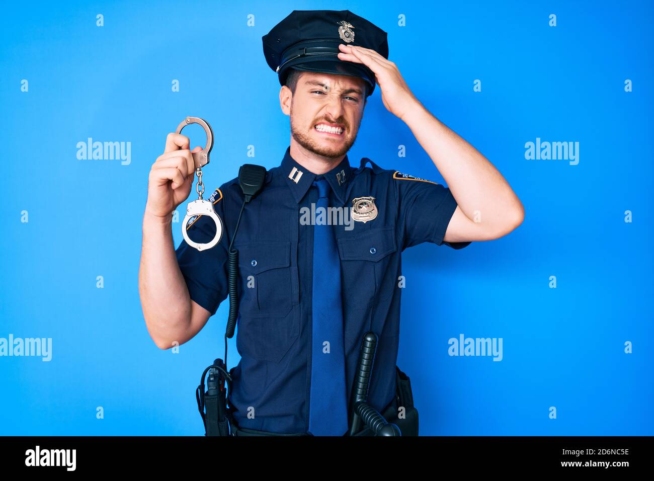 Young caucasian man wearing police uniform holding handcuffs stressed ...