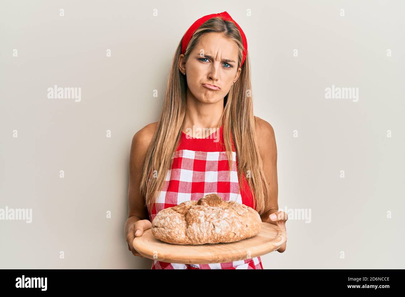 Young blonde woman wearing baker uniform holding homemade bread ...