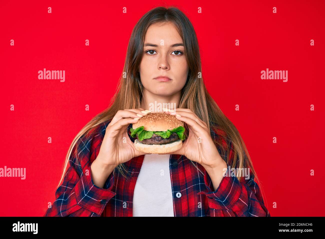 Beautiful caucasian woman eating a tasty classic burger relaxed with ...