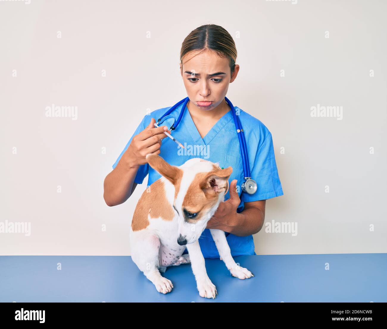 Young beautiful blonde veterinarian woman putting vaccine to puppy dog ...