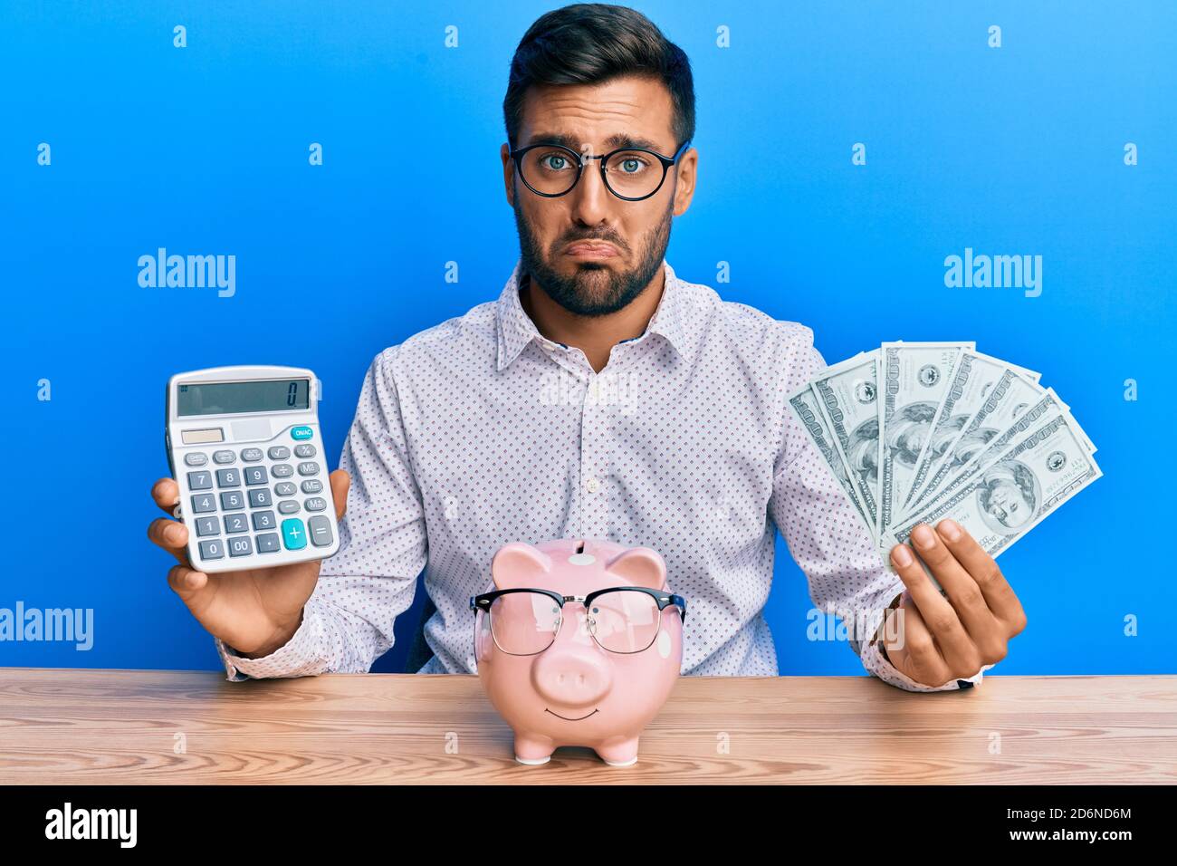 Handsome hispanic man holding dollars calculating savings depressed and ...