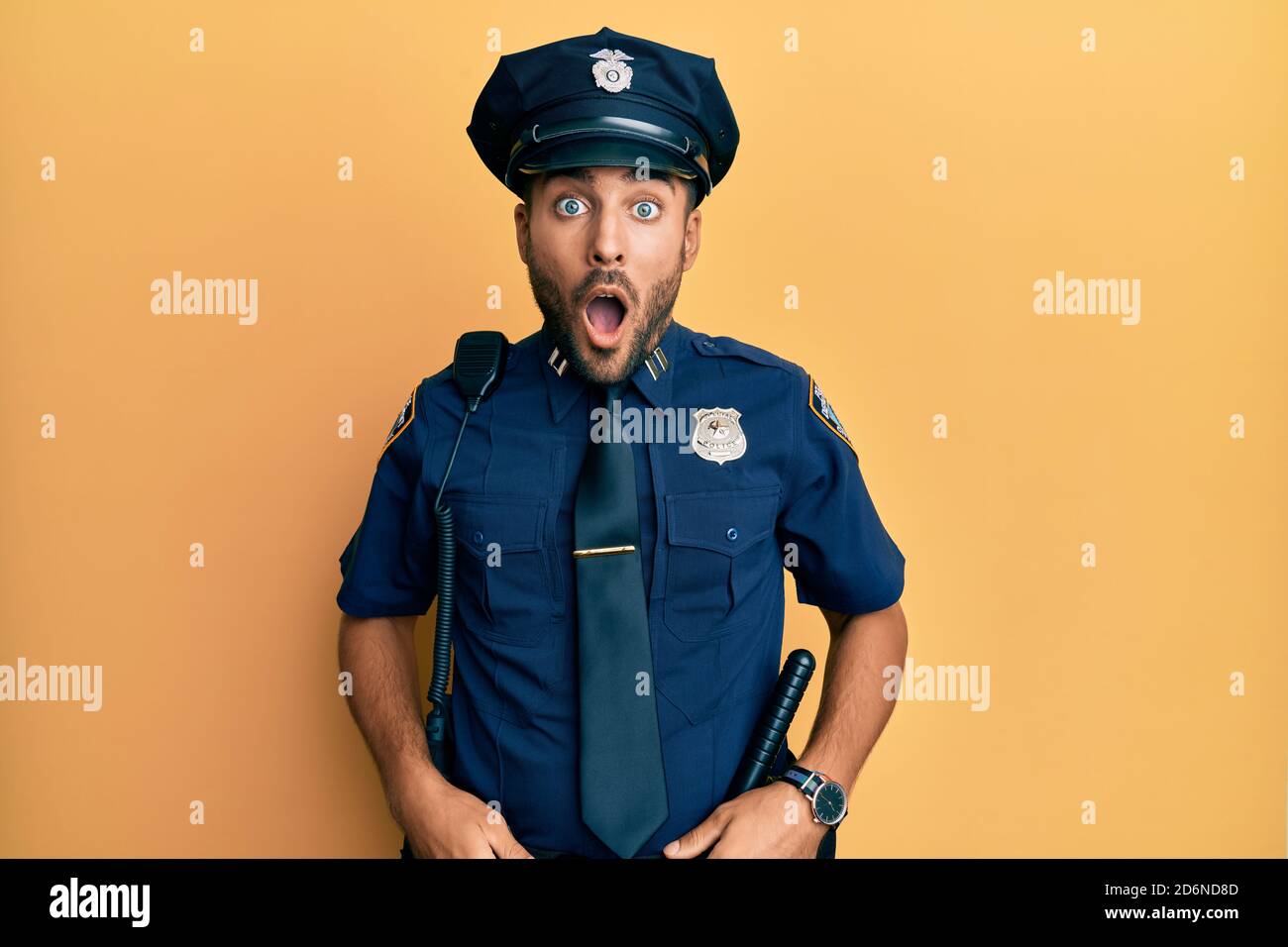 Handsome hispanic man wearing police uniform afraid and shocked with ...