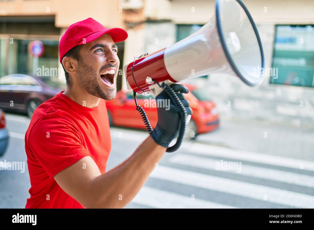 Young handsome delivery man screaming using megaphone at town street ...
