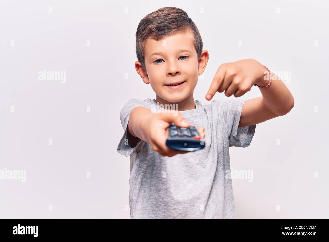 Cute blond kid holding television remote control smiling happy pointing ...