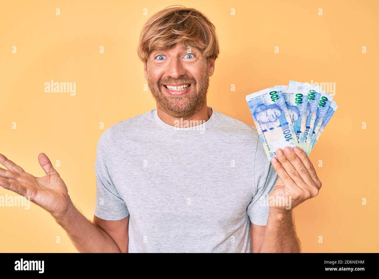 Young blond man holding south african rand banknotes celebrating ...
