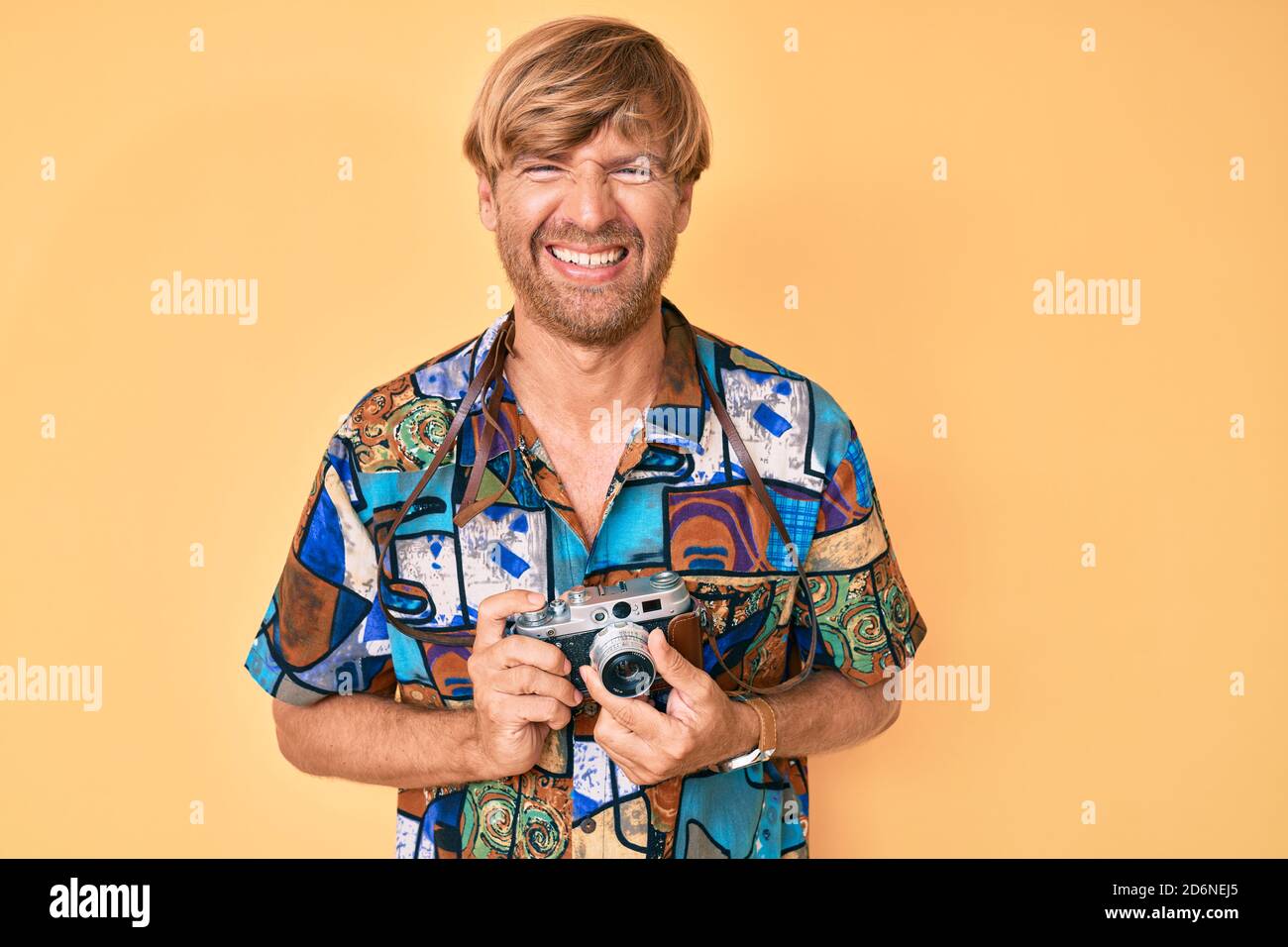 Young blond man holding vintage camera smiling and laughing hard out ...