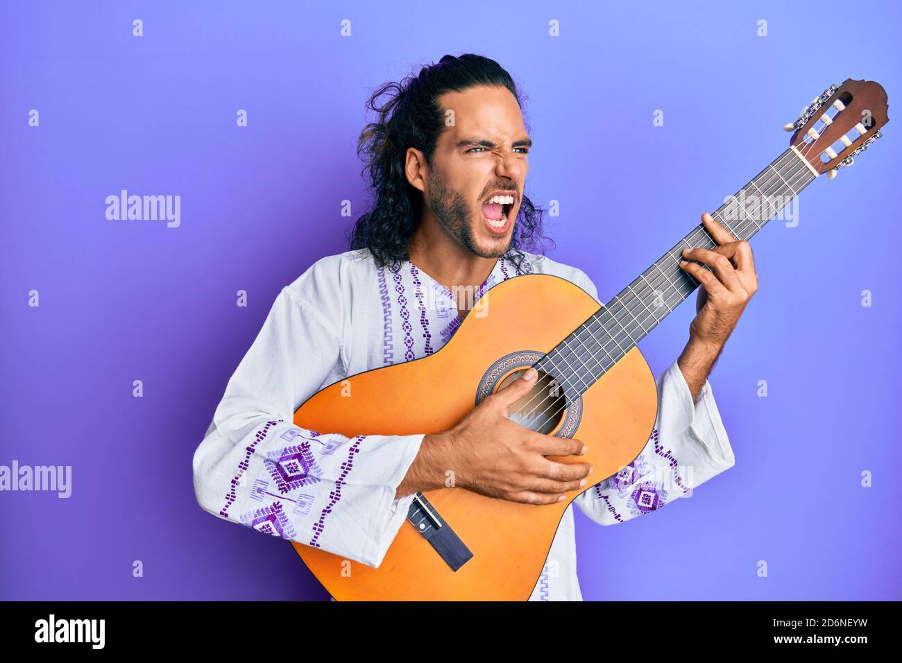 Young handsome man with long hair playing classical guitar angry and ...