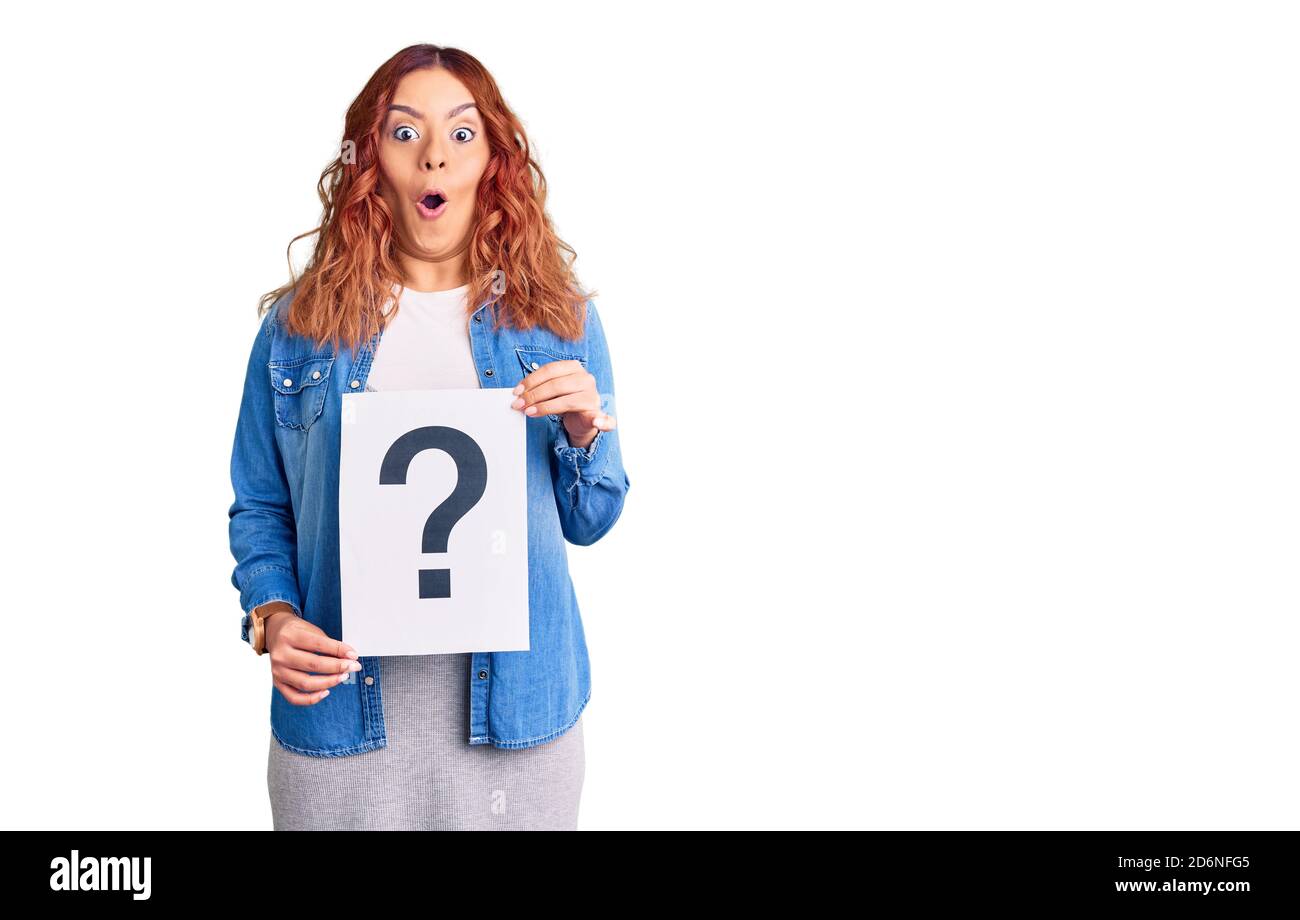 Young latin woman holding question mark scared and amazed with open ...