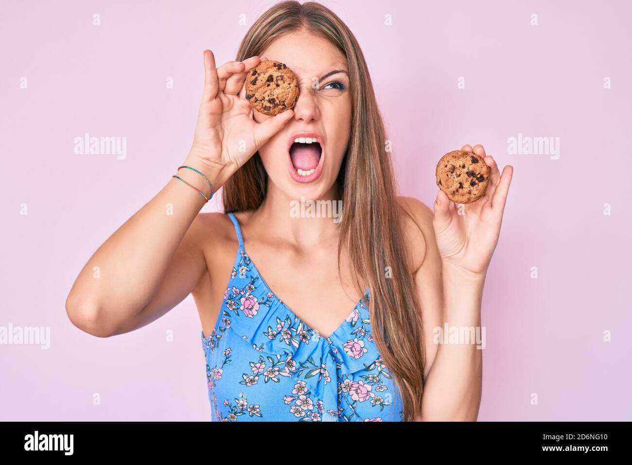 Young blonde girl holding cookie angry and mad screaming frustrated and ...