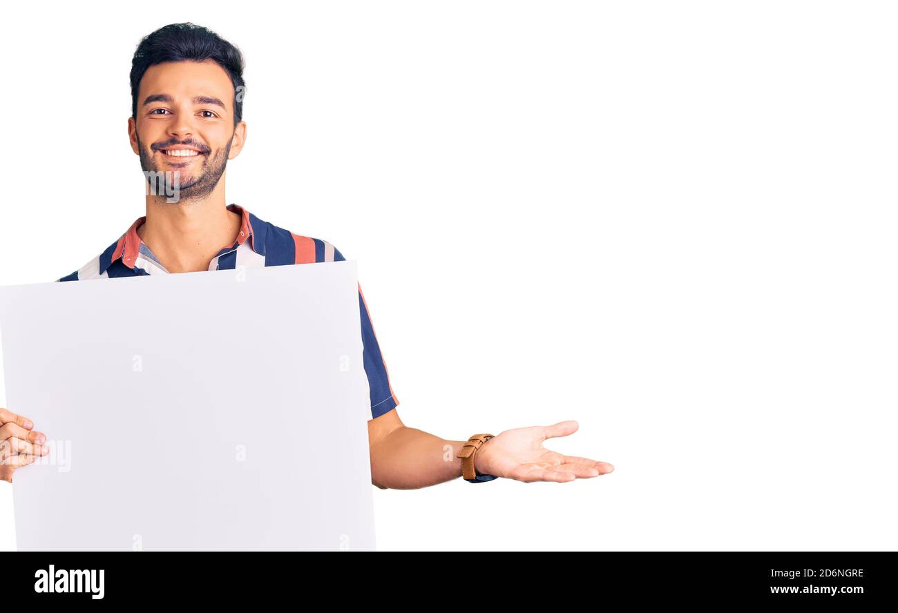 Young handsome hispanic man holding cardboard banner with blank space ...