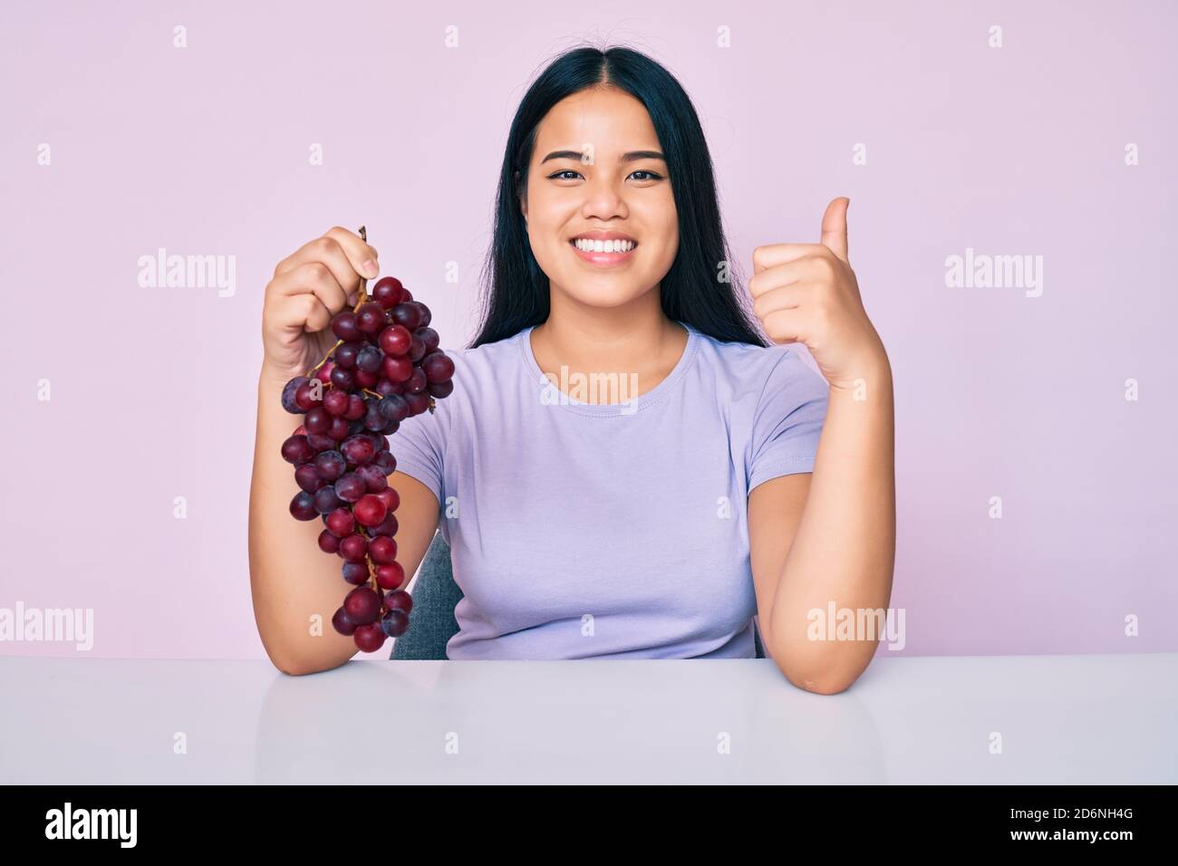 Young beautiful asian girl holding branch of fresh grapes smiling happy ...