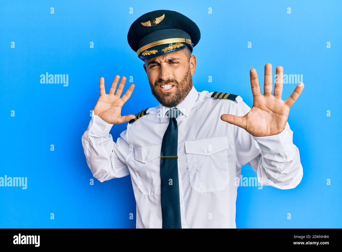 Handsome man with beard wearing airplane pilot uniform afraid and ...