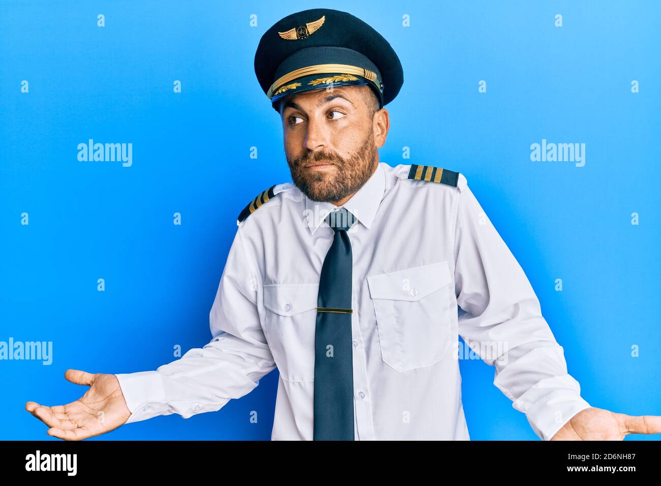 Handsome man with beard wearing airplane pilot uniform clueless and ...