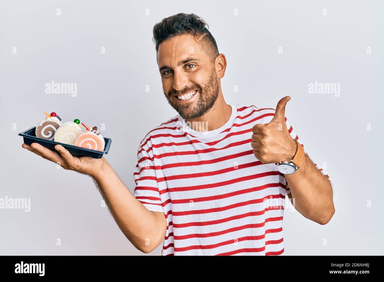 Handsome man with beard holding cake sweets smiling happy and positive ...