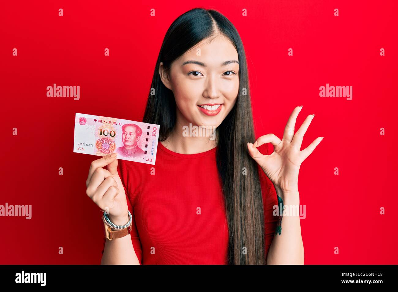 Young chinese woman holding 100 yuan chinese banknote doing ok sign ...