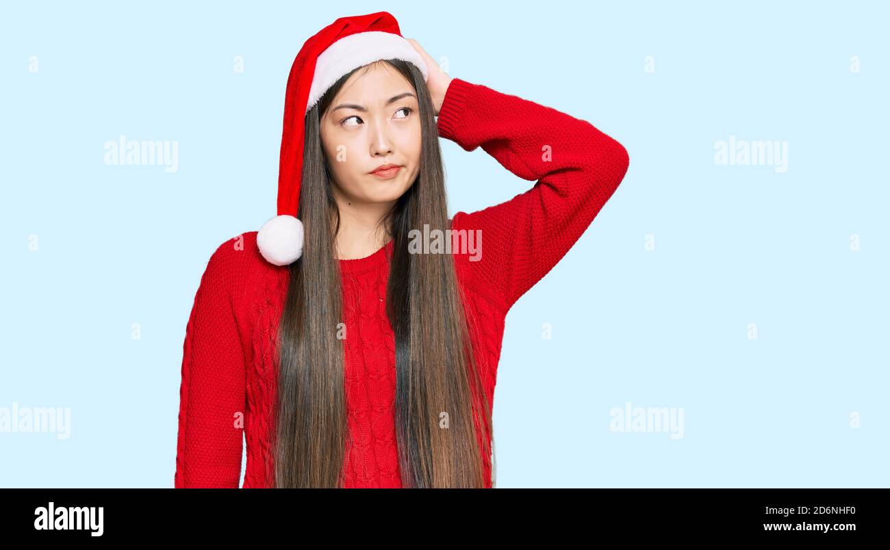 Young chinese woman wearing christmas hat confuse and wondering about ...