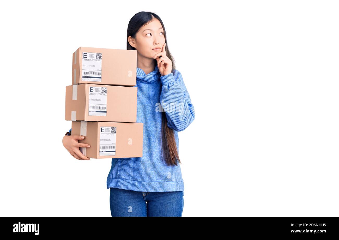 Young beautiful chinese woman holding delivery cardboard boxes serious ...