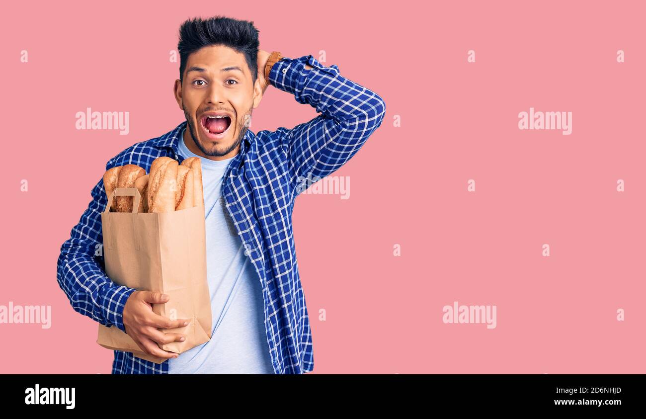Handsome latin american young man holding paper bag with bread crazy ...