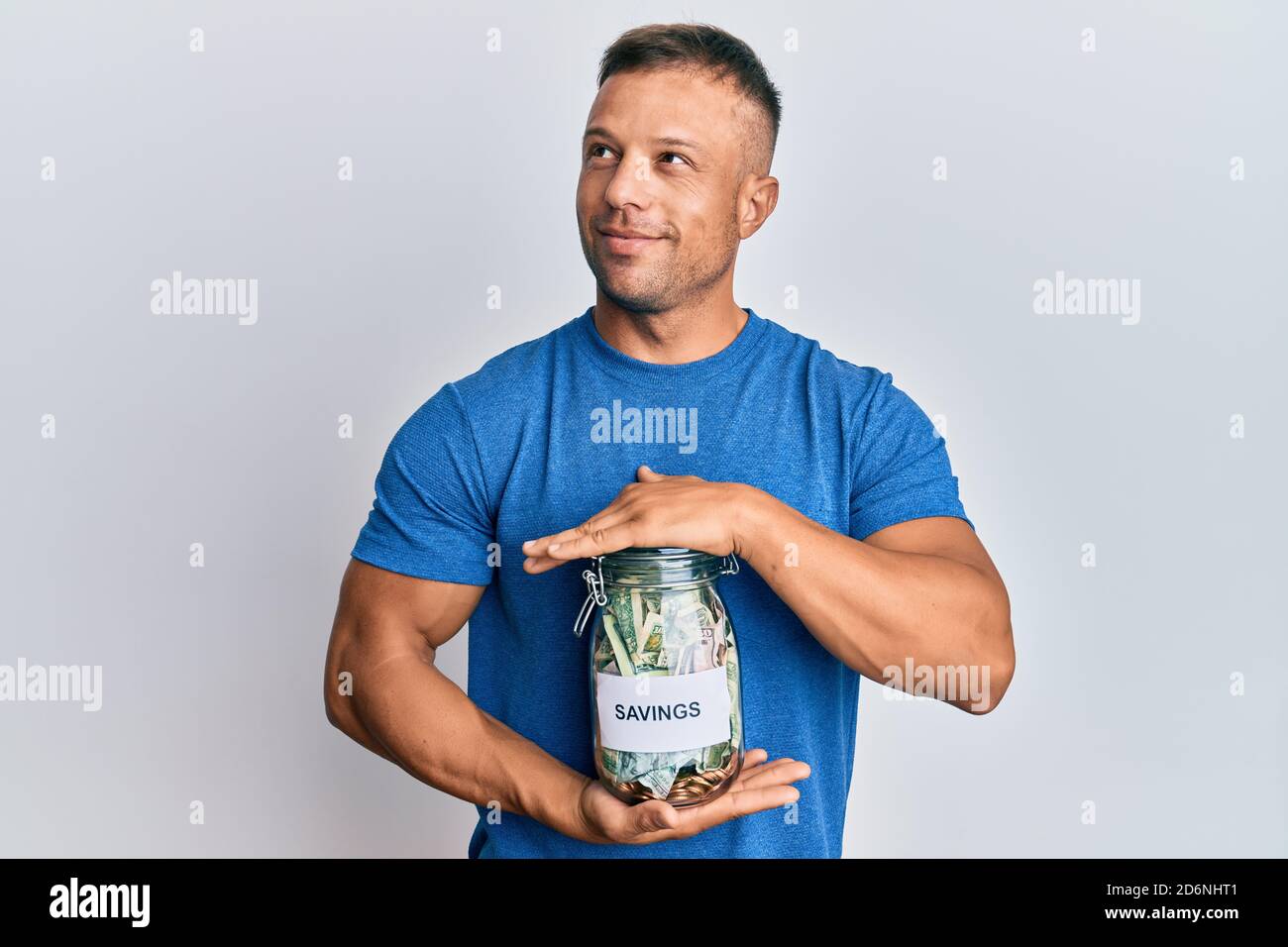 Handsome muscle man holding jar with savings smiling looking to the ...