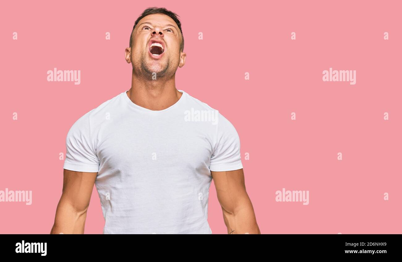 Handsome muscle man wearing casual white tshirt angry and mad screaming ...