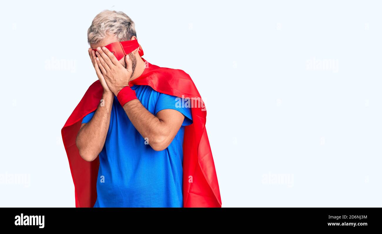 Young blond man wearing super hero custome with sad expression covering ...