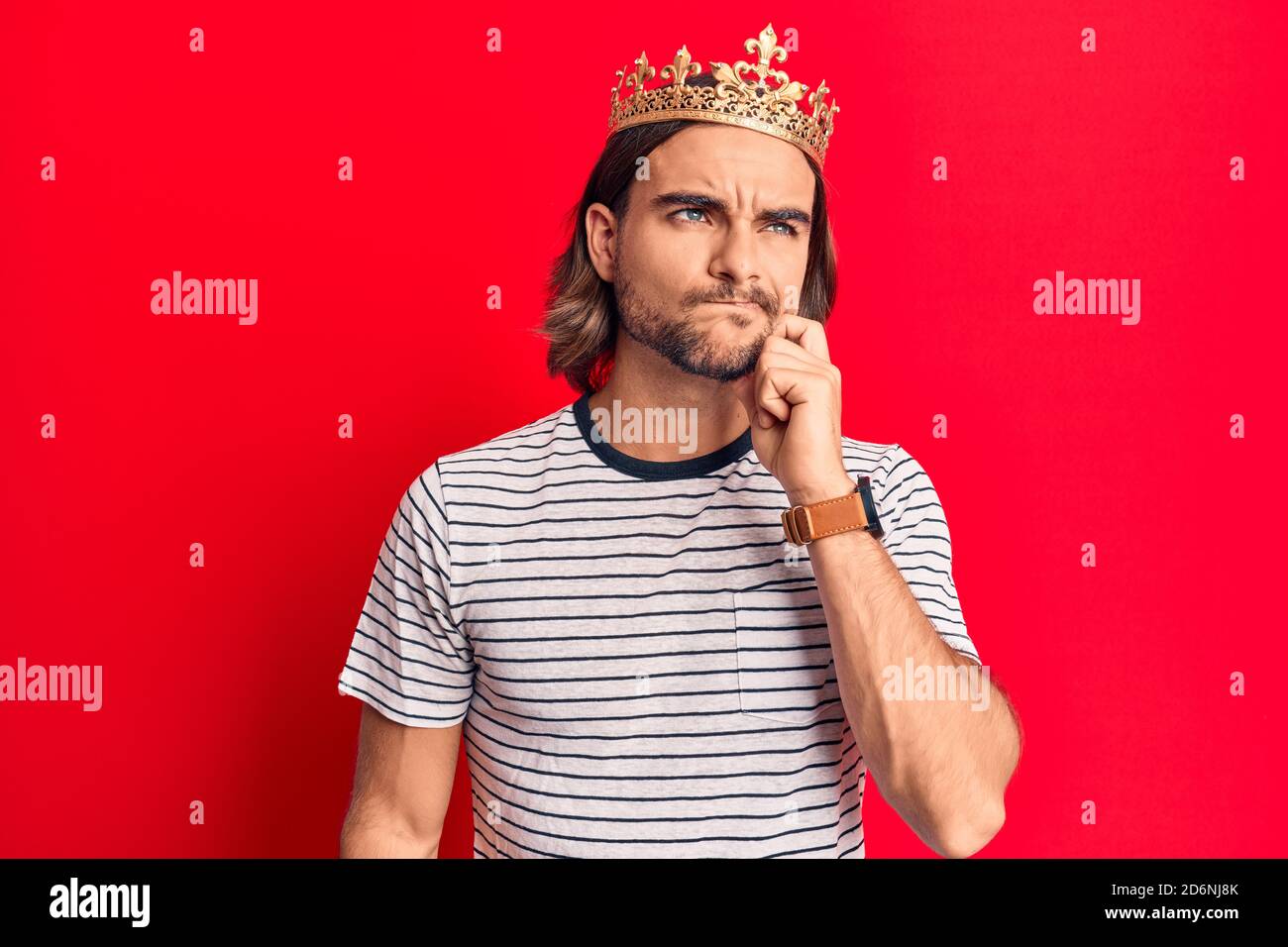 Young handsome man wearing prince crown thinking concentrated about ...