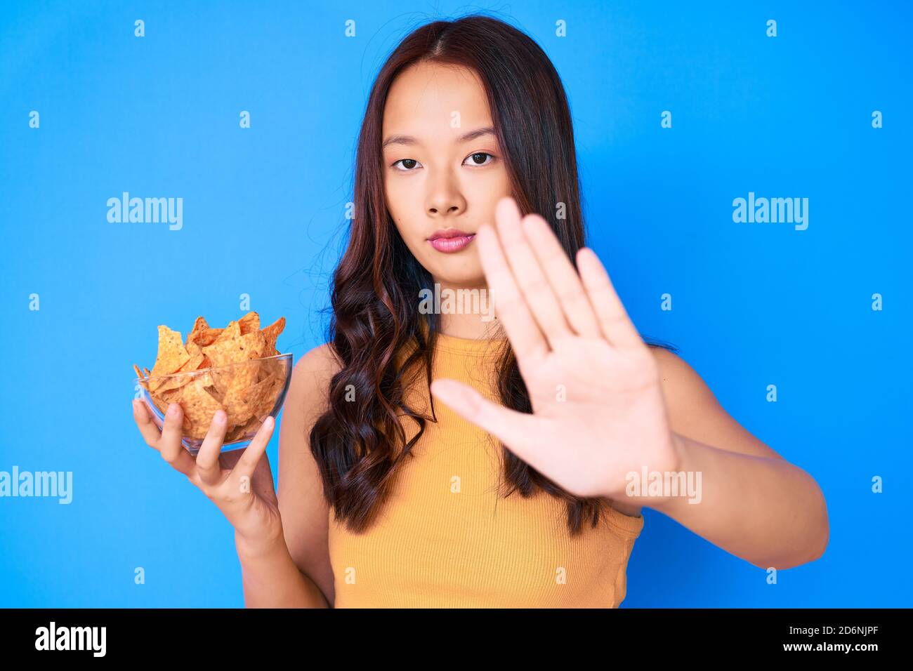 Young beautiful chinese girl holding nachos potato chips with open hand ...