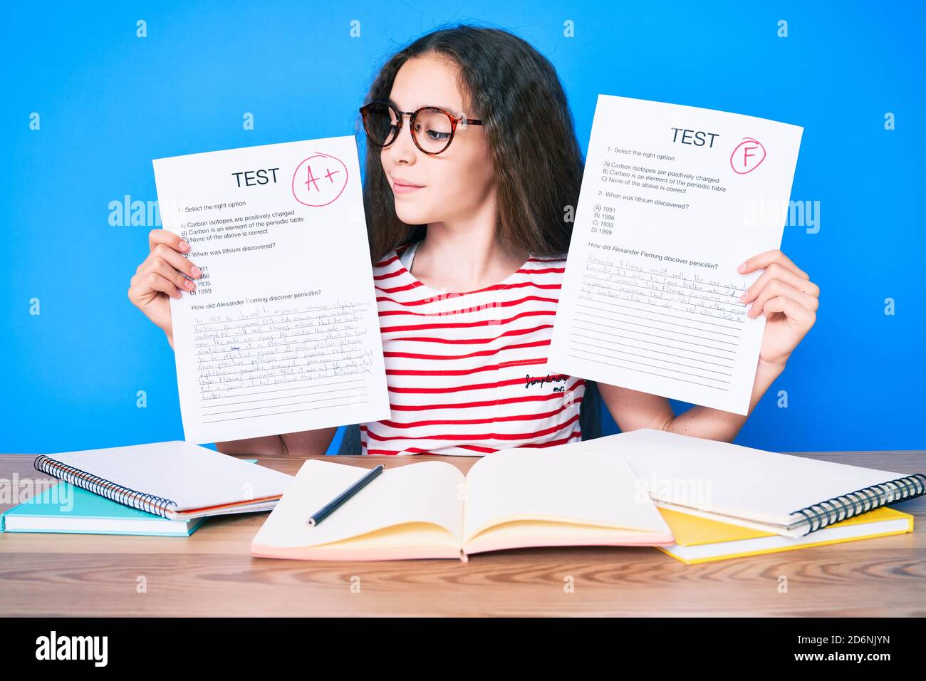 Cute hispanic girl showing failed and passe exam sitting on the table ...