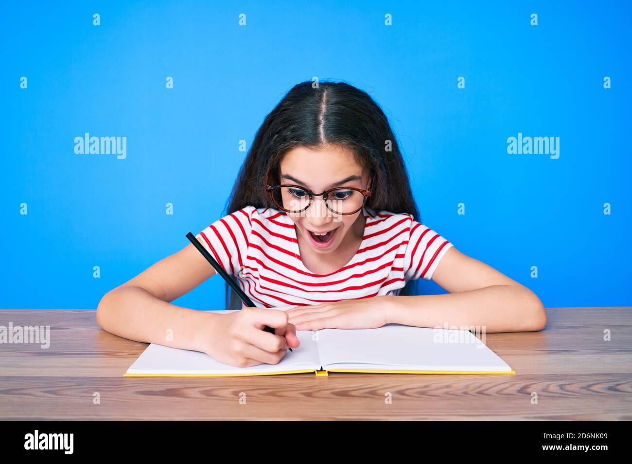 Cute hispanic child girl sitting on the table writing book scared and ...