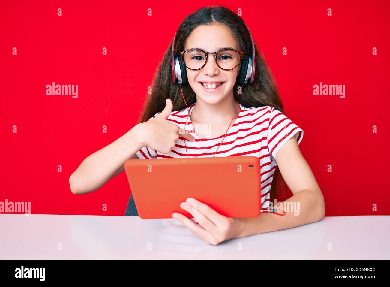 Cute hispanic child girl using touchpad and headphones sitting on the ...
