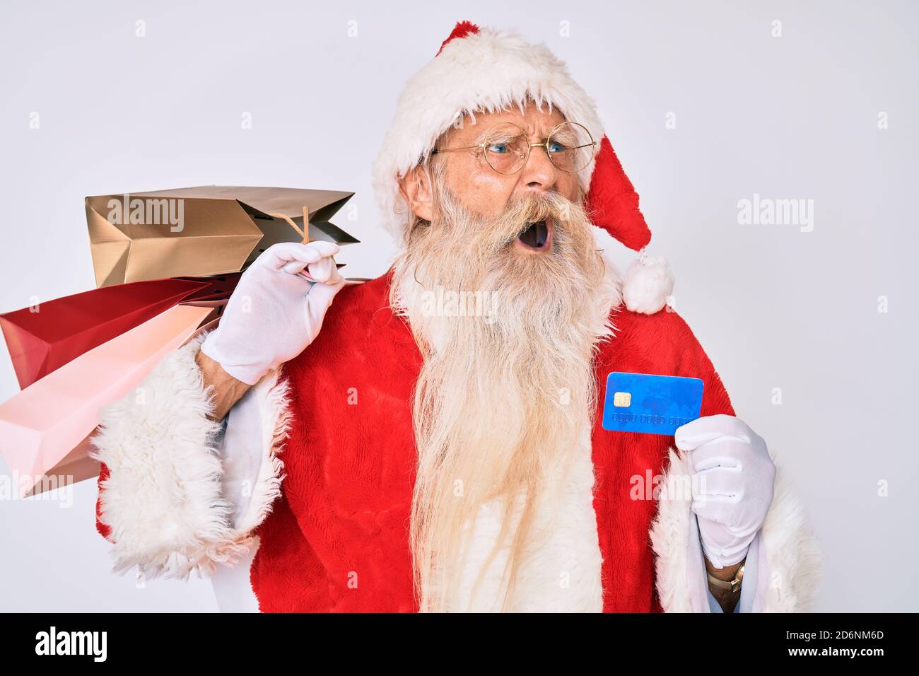 Old senior man wearing santa claus costume holding shopping bags and ...