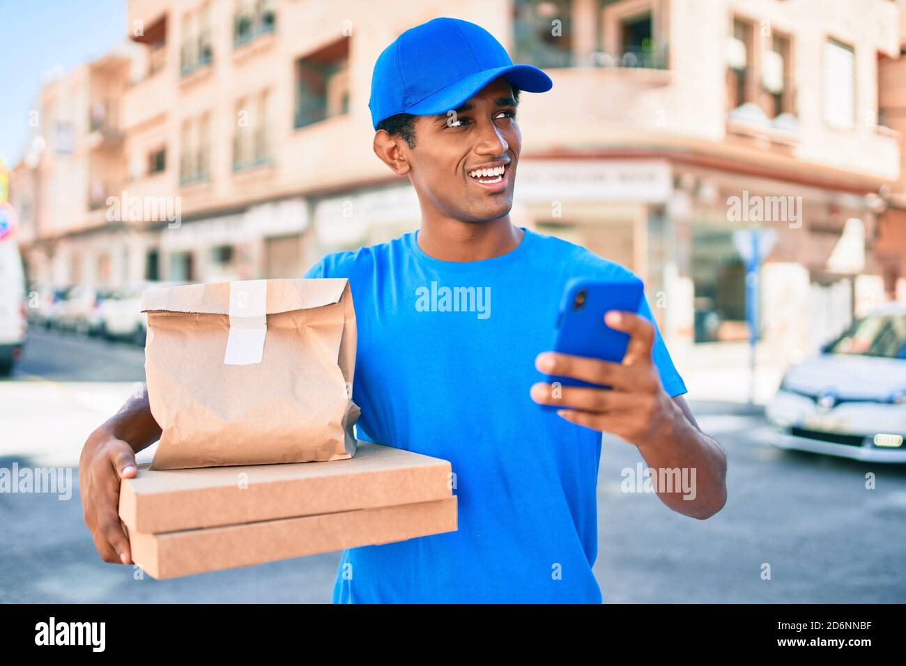 African delivery man wearing courier uniform outdoors using smartphone ...
